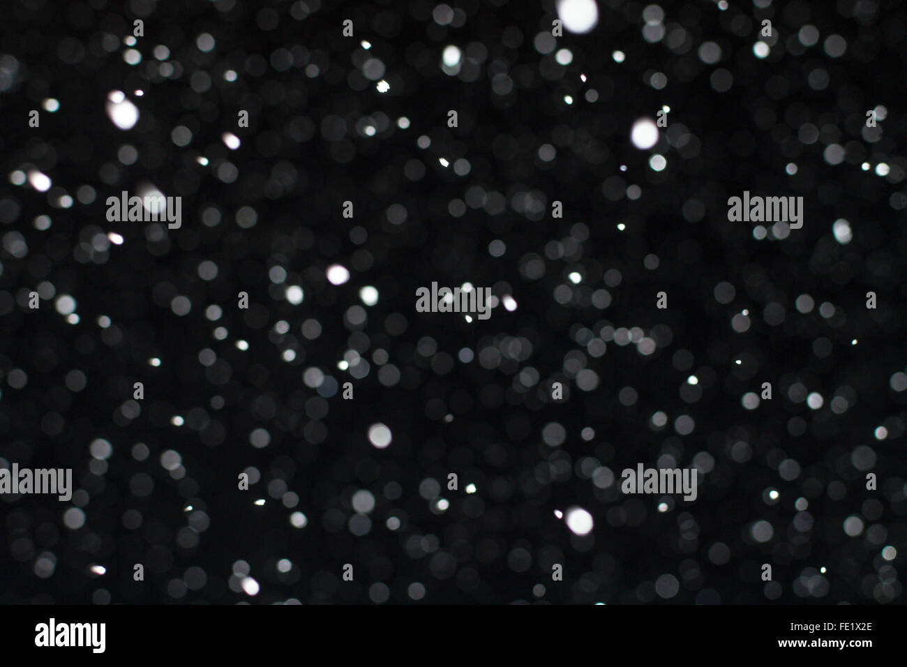 Flakes of natural snow falling at night set against a black background ...