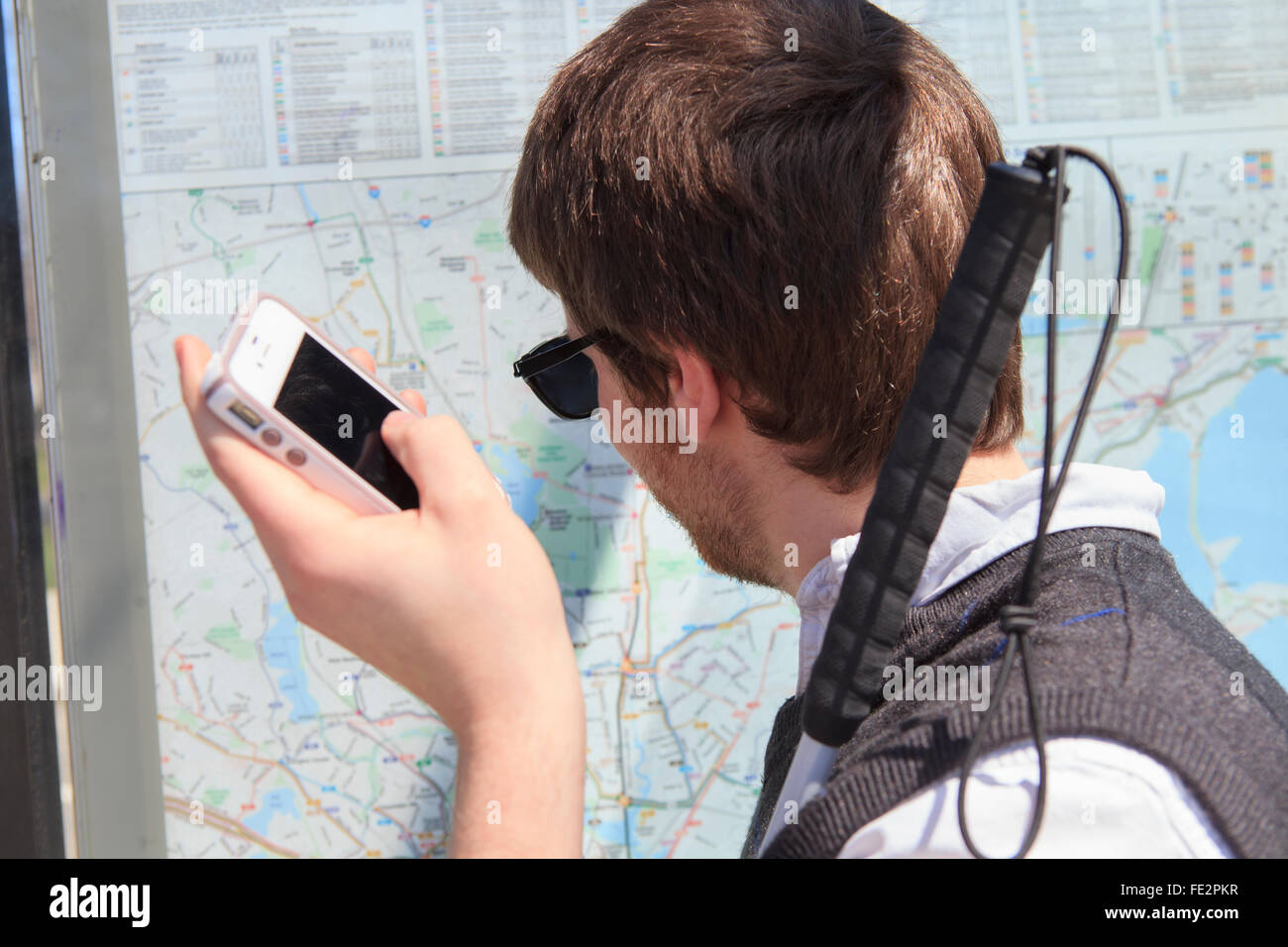 Young blind man at a bus stop using assistive technology to help with ...