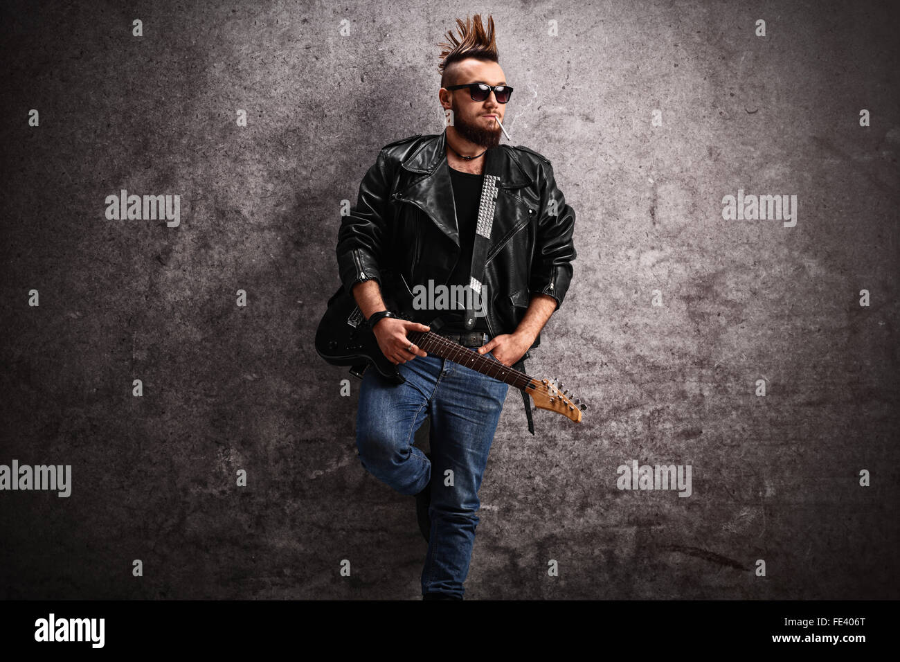 Young punk rocker holding an electric guitar and leaning against a ...