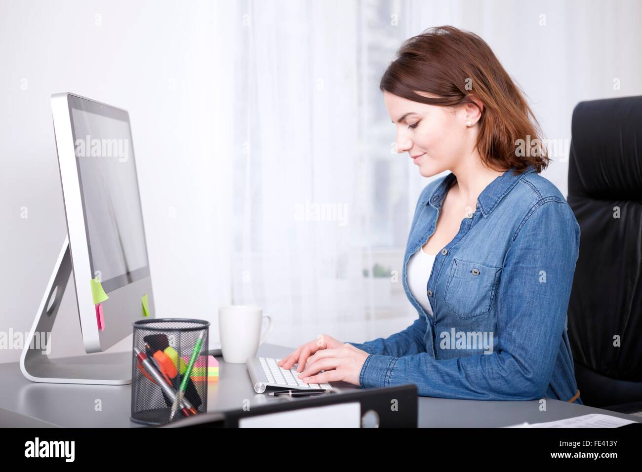 Smiling businesswoman inputting data to her desktop computer sitting ...