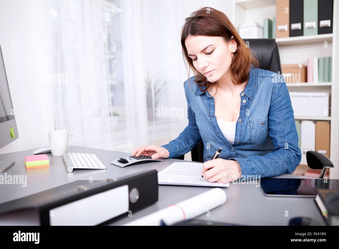 Hardworking businesswoman sitting at her desk in the office writing a ...