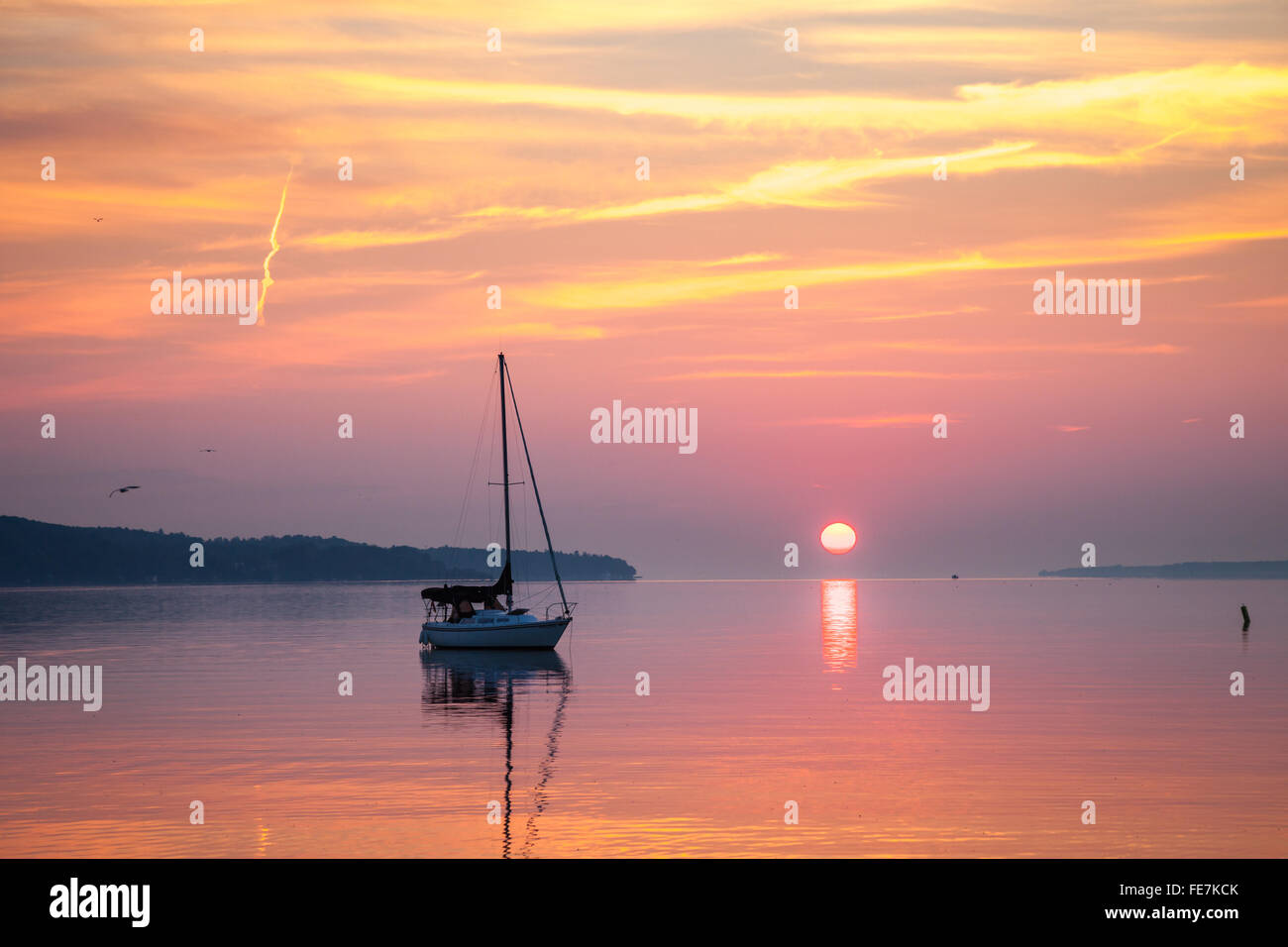 Waterfront scene of a Sailboat at sunrise, with a reflection in the ...
