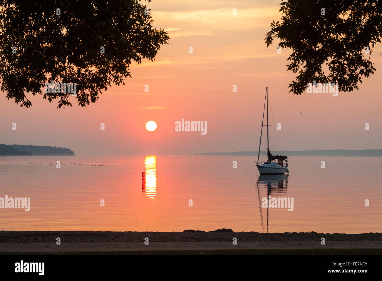 Waterfront scene of a Sailboat at sunrise, with a reflection in the ...