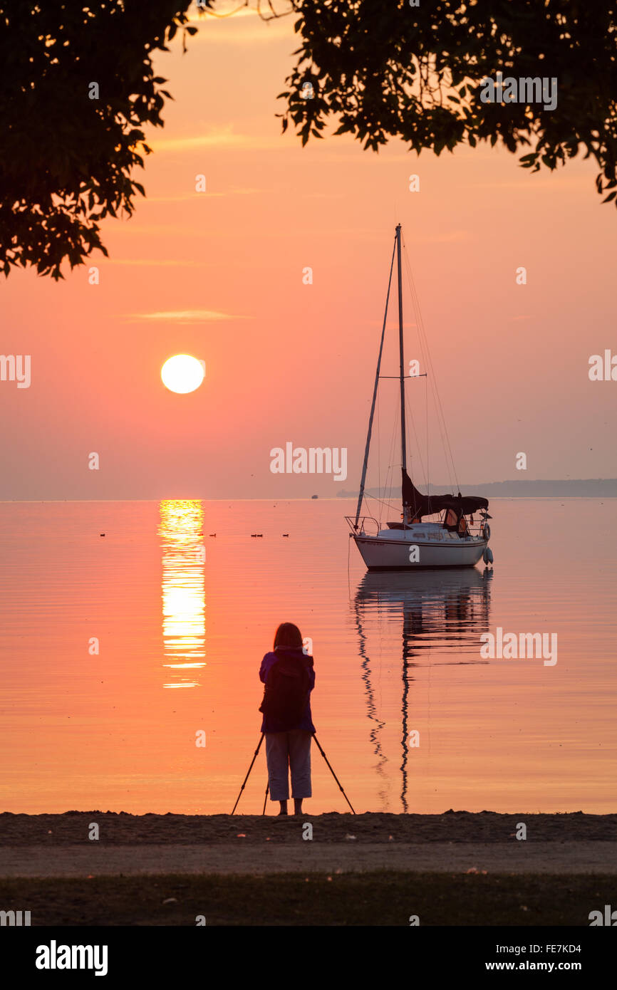 Waterfront scene of a Sailboat and photographer at sunrise, with a ...
