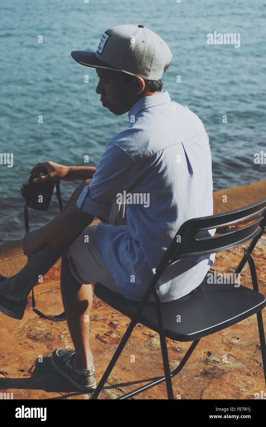Boy Sitting On Chair At Harbor Stock Photo - Alamy