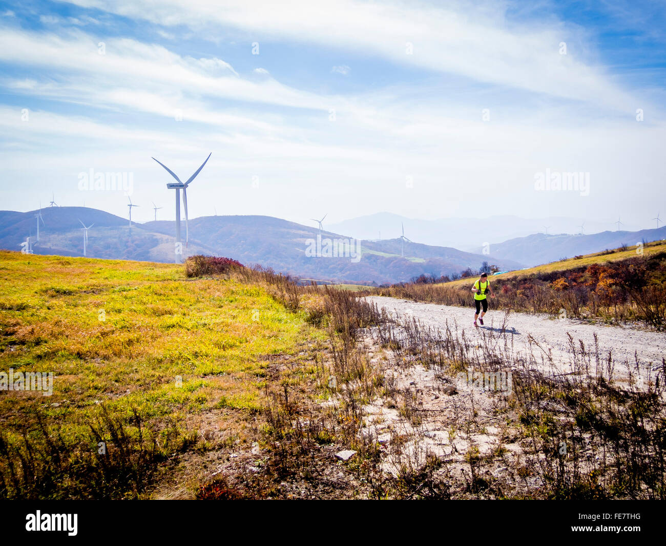 A trail runner runs along a ridge line, with wind turbines in the ...