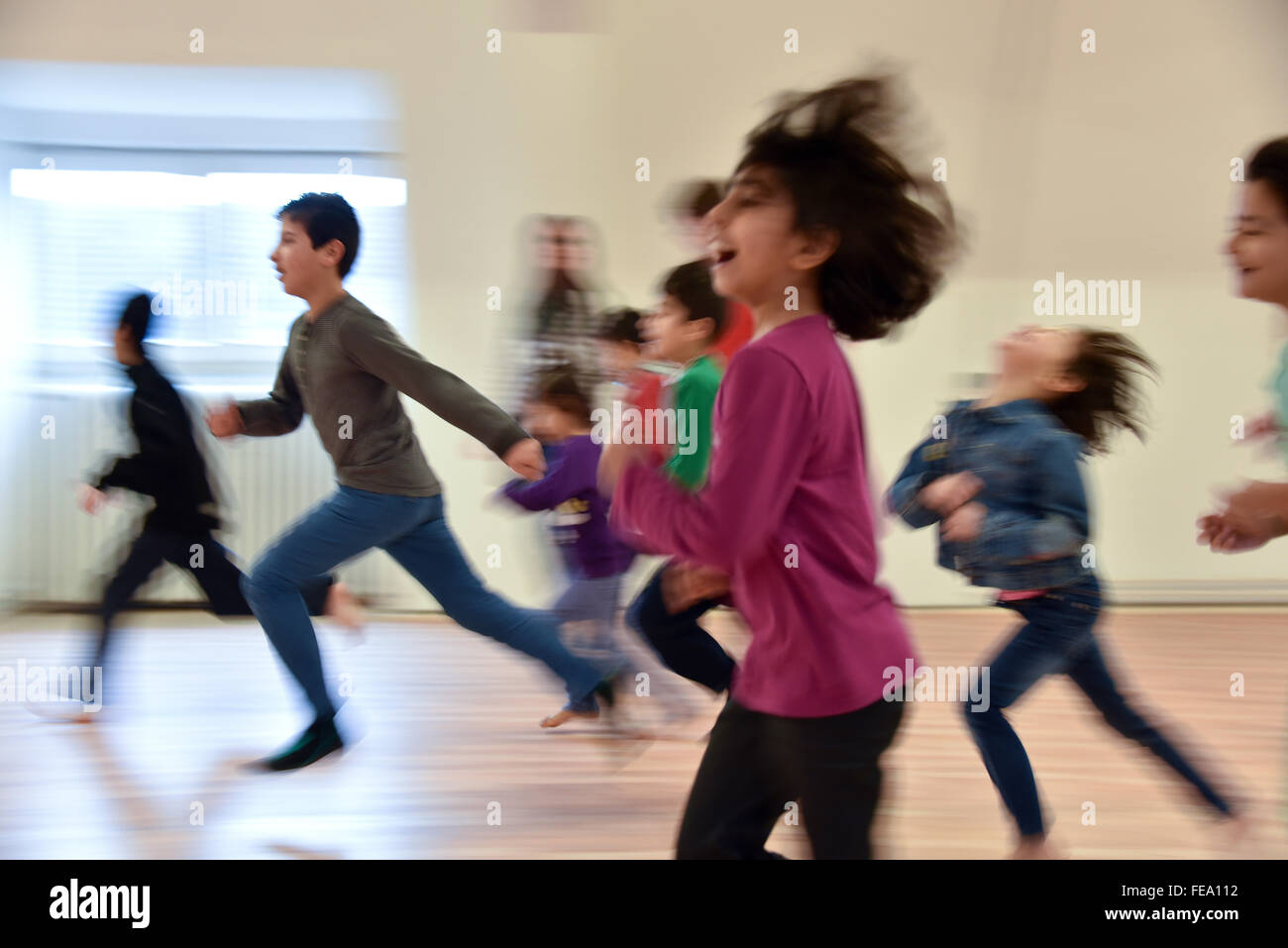 Refugee children running through a sports room as part of a child care ...