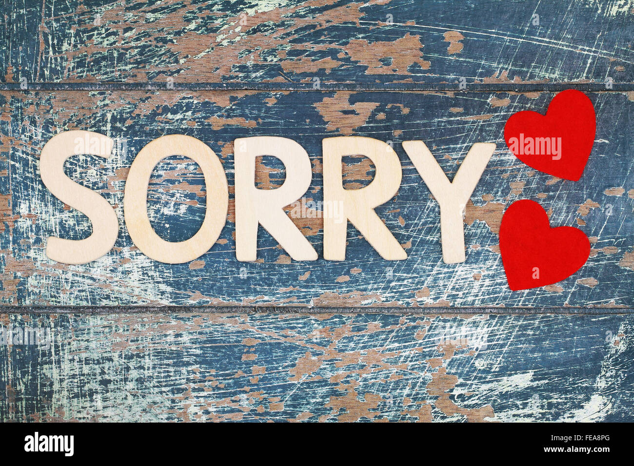 Sorry written with wooden letters and two red hearts on rustic surface ...