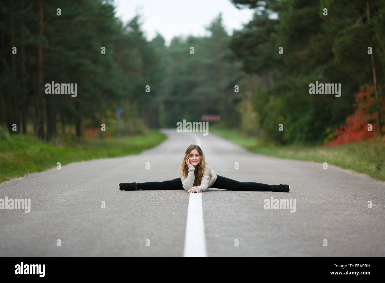 Young professional gymnast makes splits on the road at autumn time ...