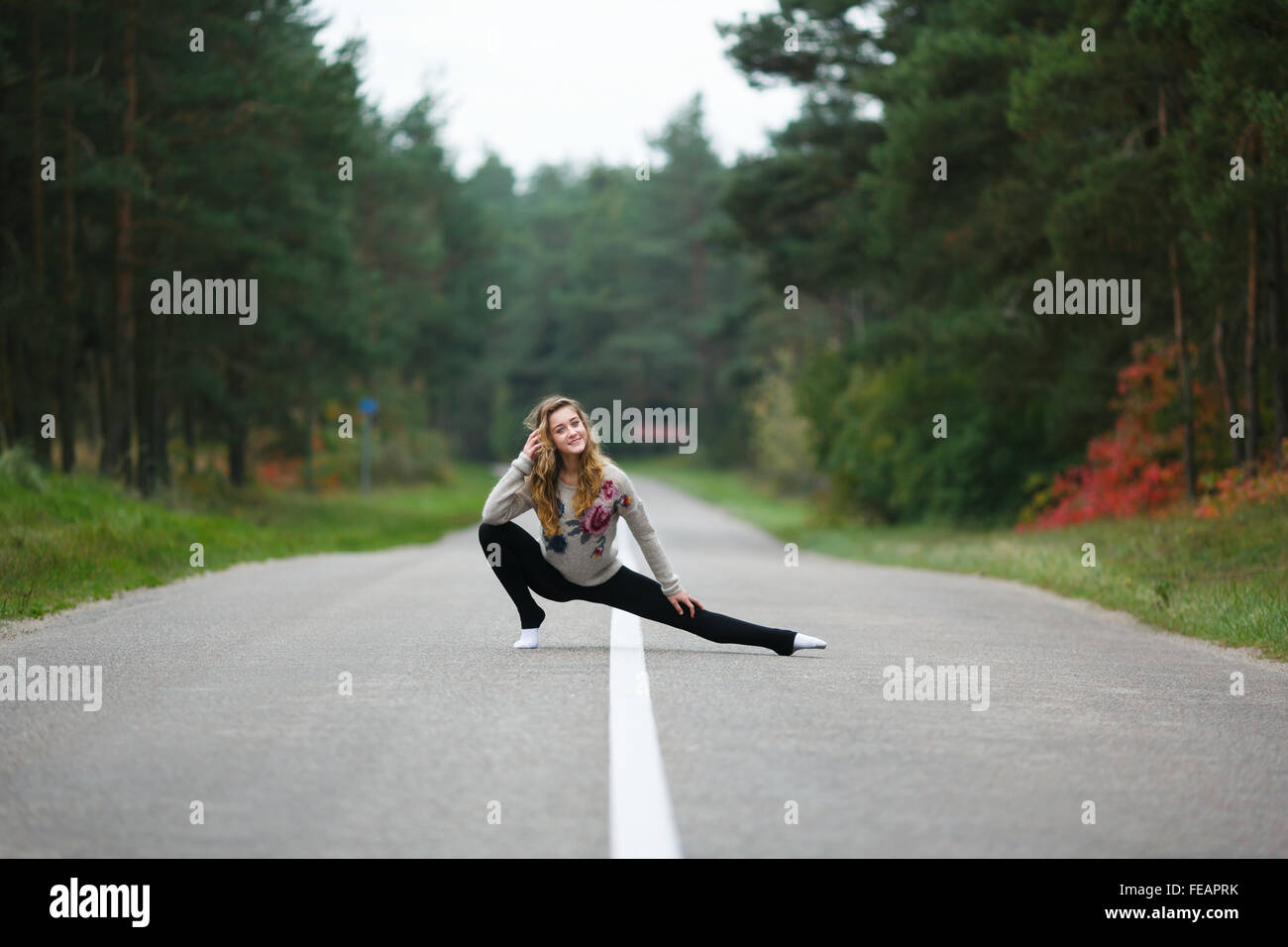 Young professional gymnast makes splits on the road at autumn time ...