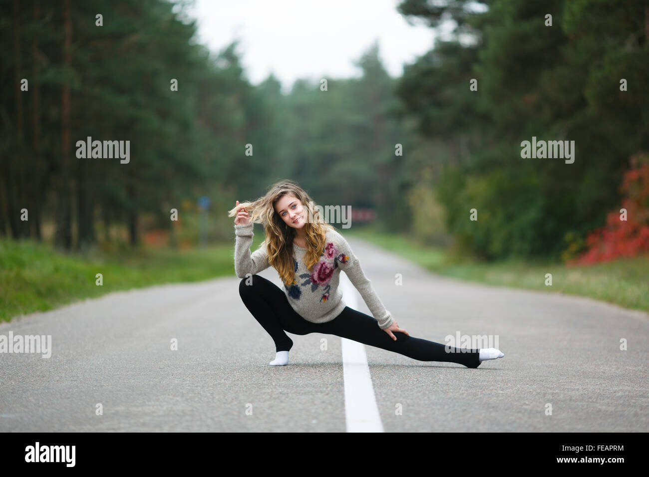 Young professional gymnast makes splits on the road at autumn time ...