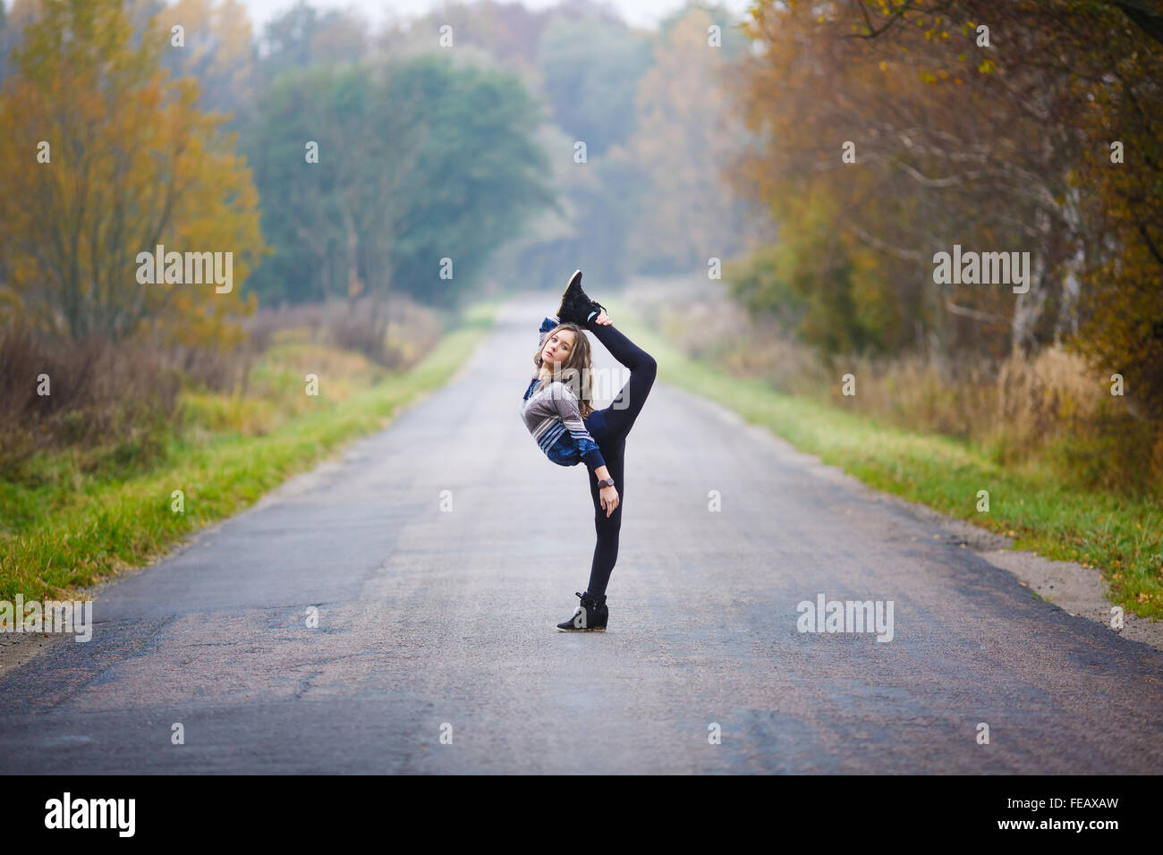 Young professional gymnast makes splits on the road at autumn time ...