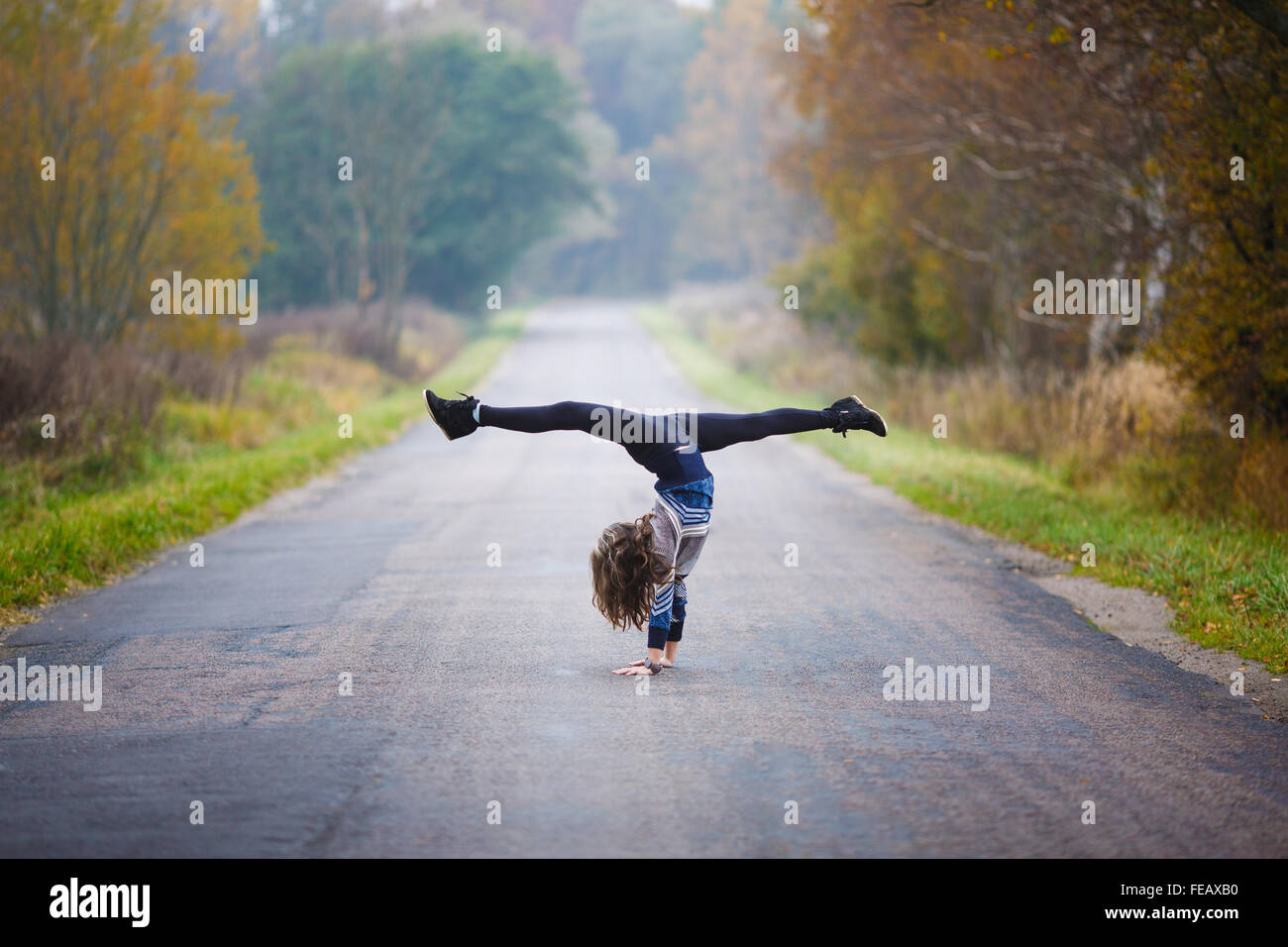Young professional gymnast makes splits on the road at autumn time ...