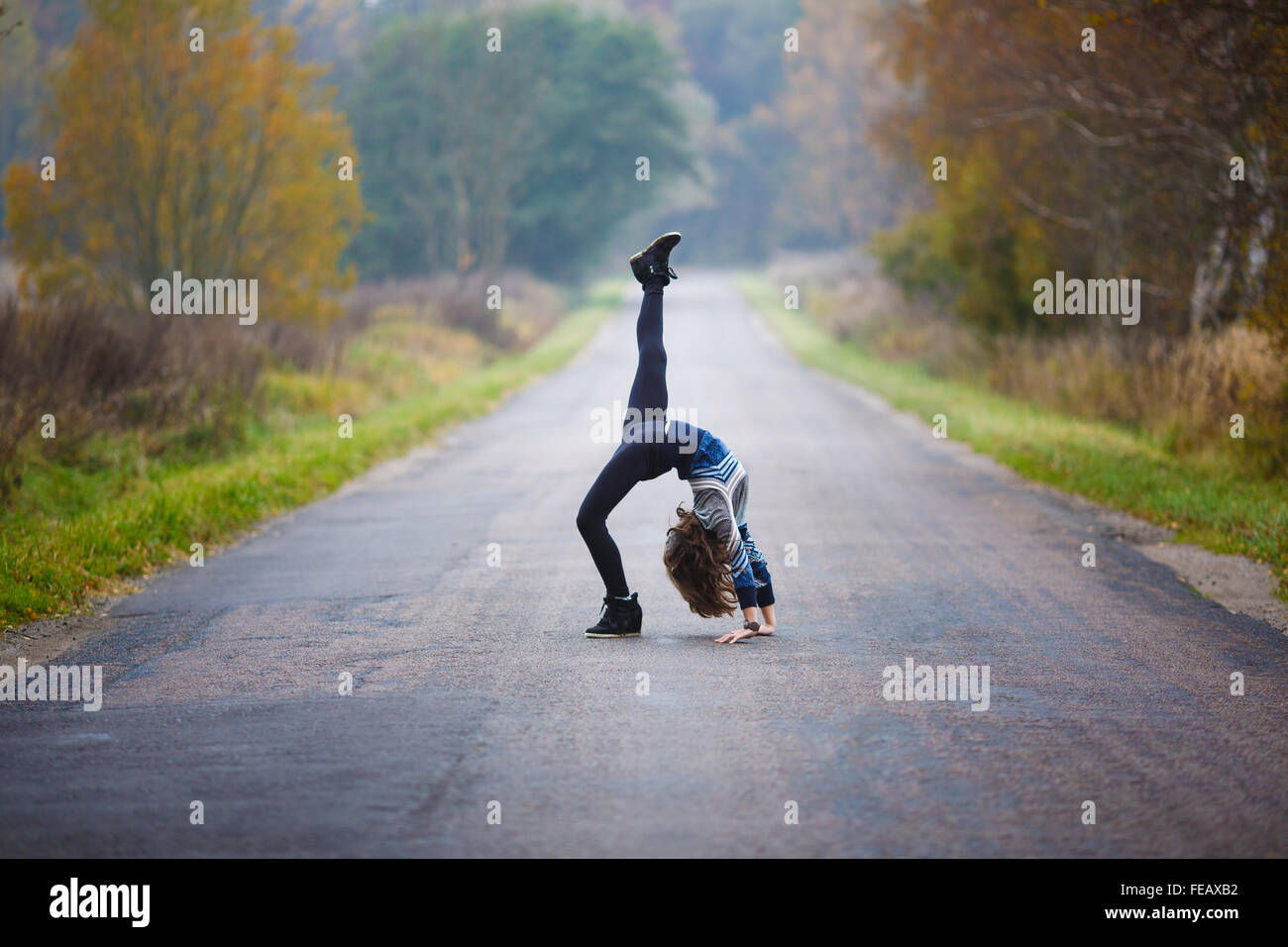 Young professional gymnast makes splits on the road at autumn time ...