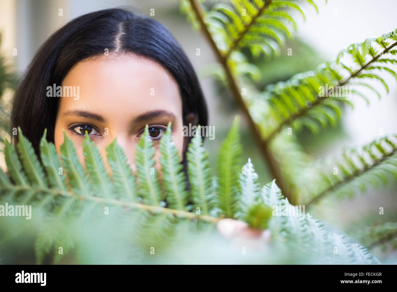 Portrait of a pretty woman looking through leaves Stock Photo - Alamy