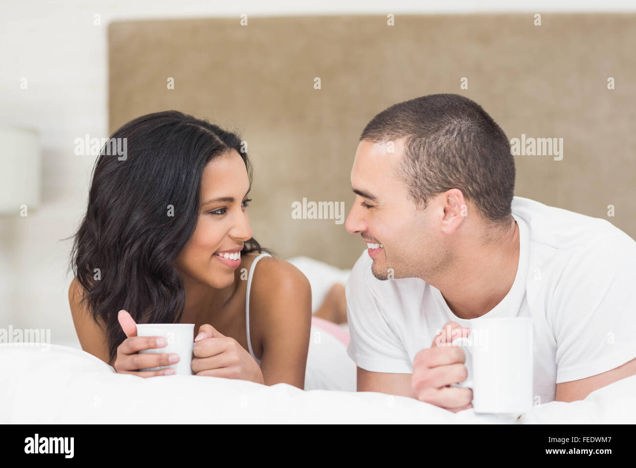Smiling couple drinking coffee lying on the bed Stock Photo - Alamy