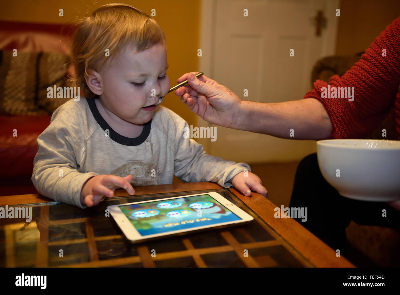 An eighteen month old toddler being spoon fed while playing a game on ...