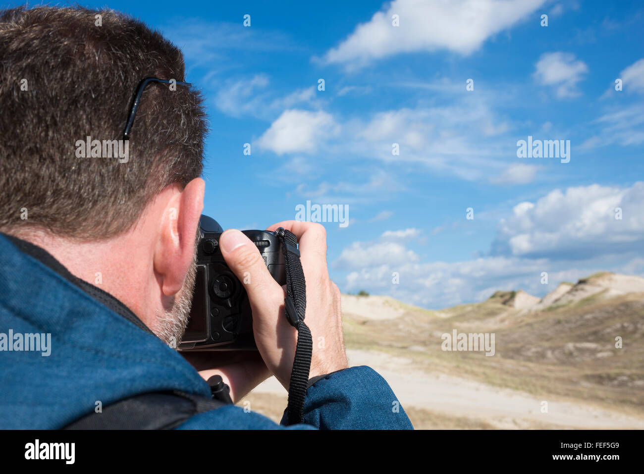 Rear view of a photographer taking pictures of sand and sky landscape ...