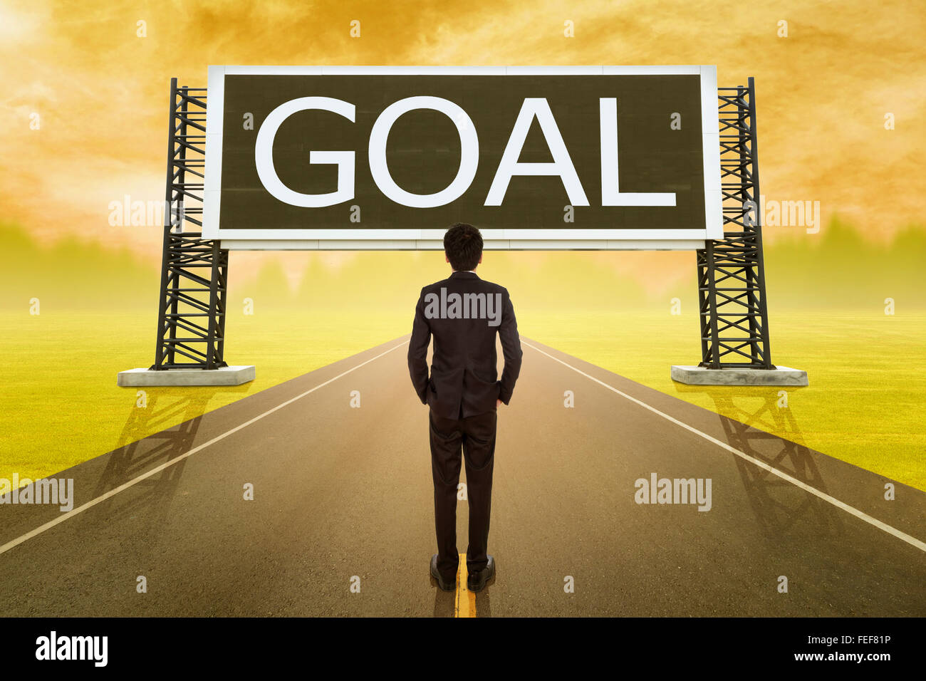 businessman standing on road and looking with large sign of goal at ...