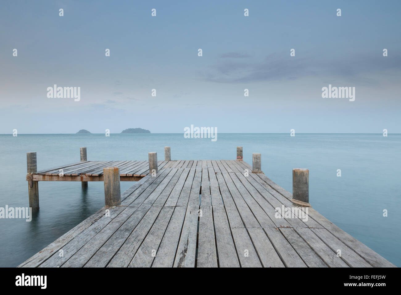 A worn wooden jetty with calm sea and pastel colors, a red buoy is just ...