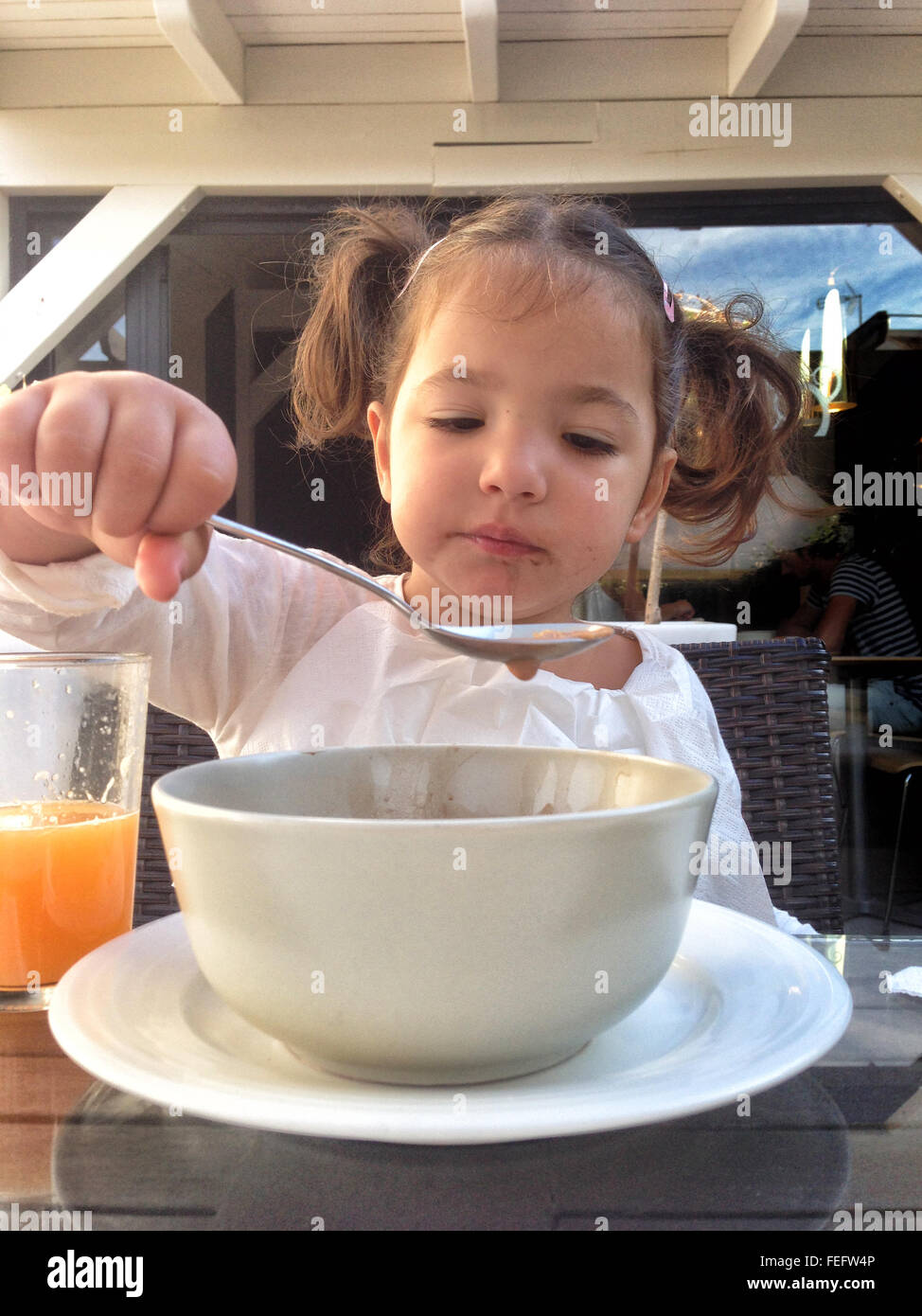 Child girl having a healthy breakfast outdoors. She is eating chocolate ...
