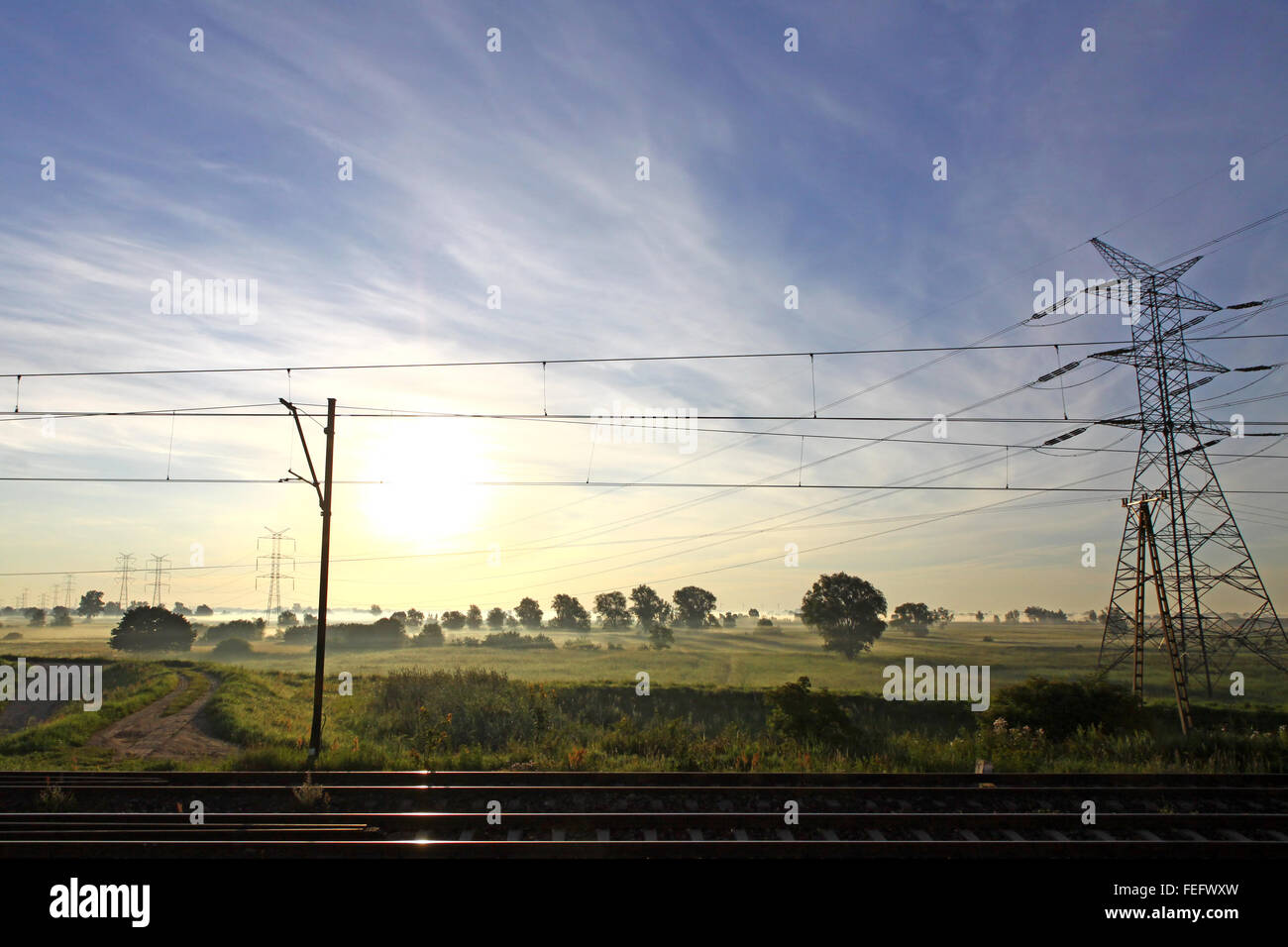 Sun rising behind electricity pylon and railroad tracks Stock Photo - Alamy