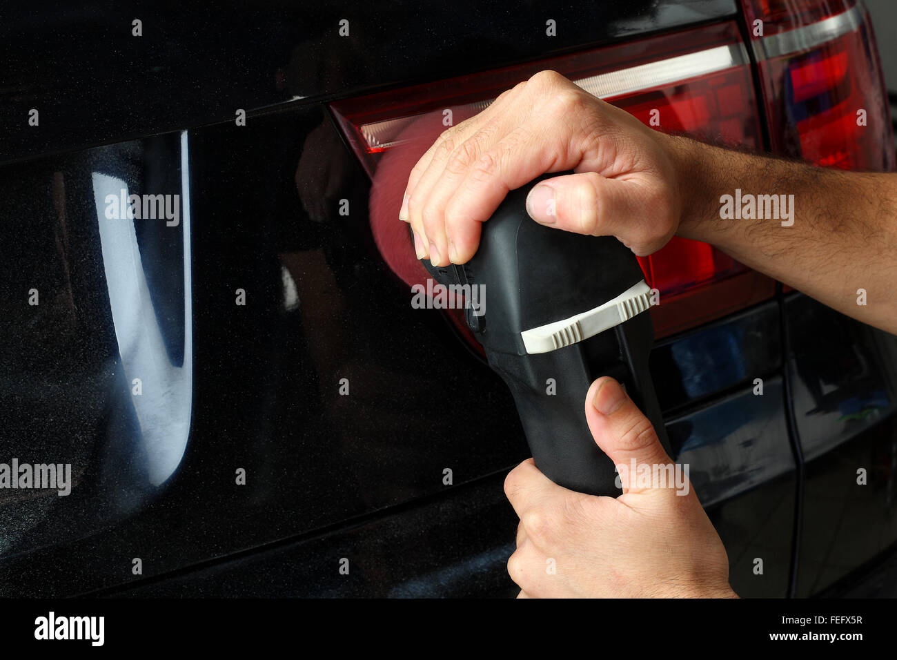 The worker polishes rear optics of headlights of the car with the ...