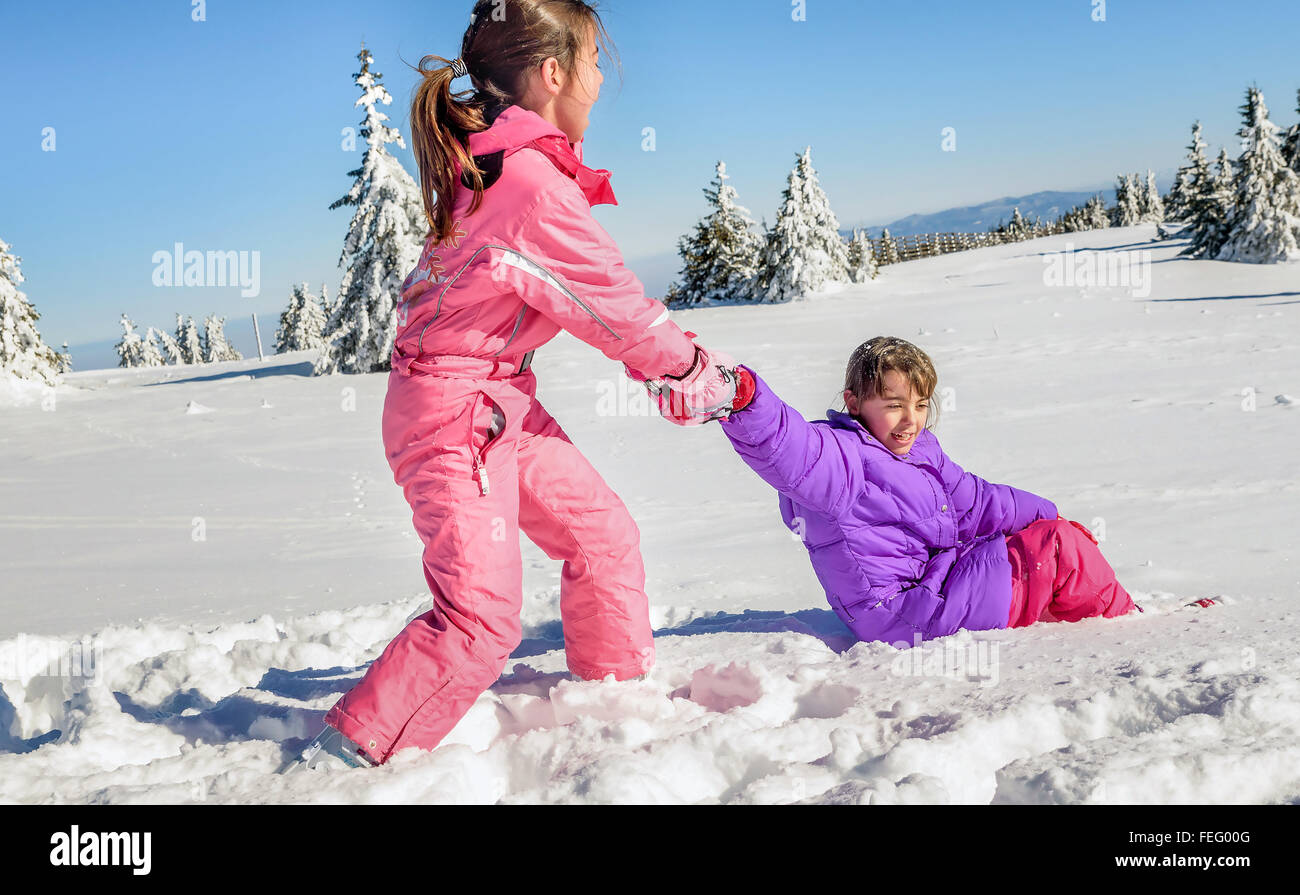 Little girl helping her friend to get up on the snow Stock Photo - Alamy