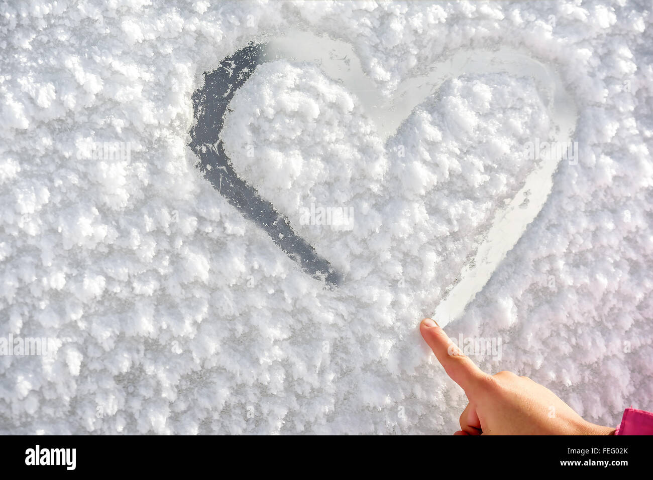 Little girl drawing heart on snow Stock Photo - Alamy