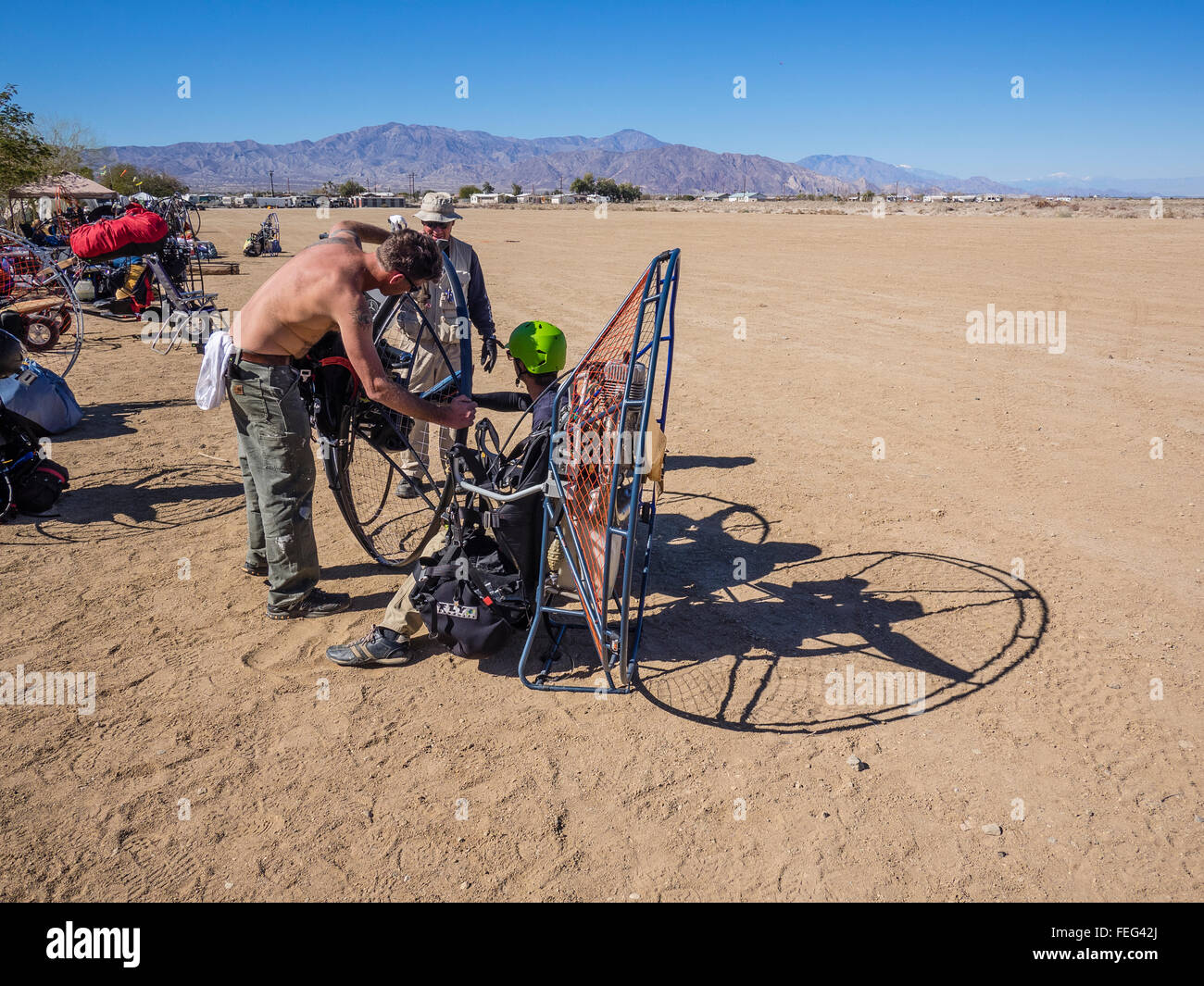 Three male paramotoring pilots work to start the engine of their ...