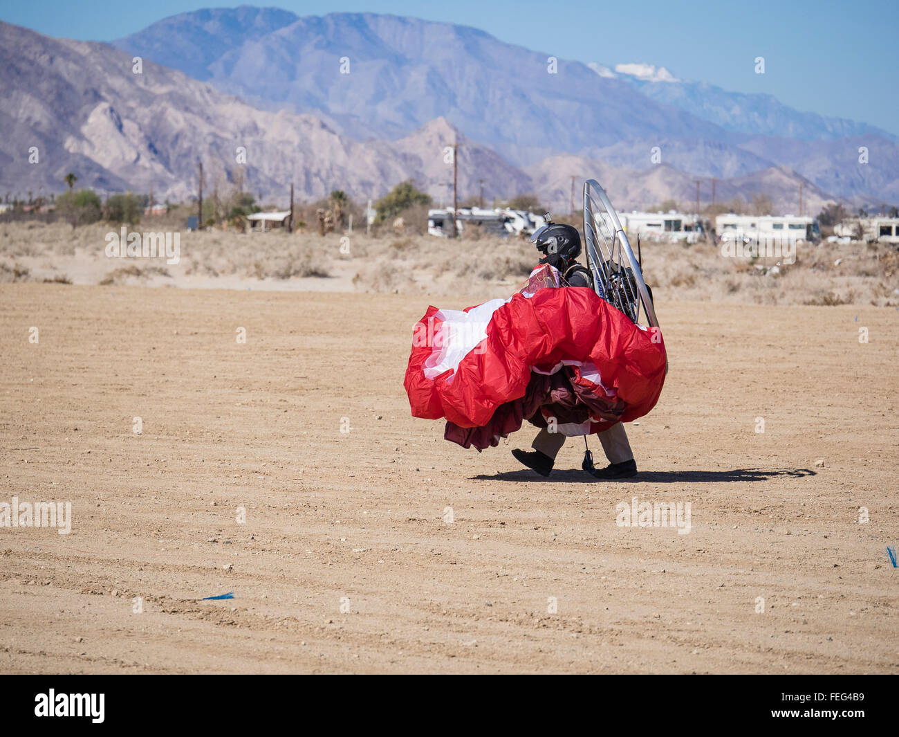 A paramotor pilot carries his paramotor on his back and holds his ...