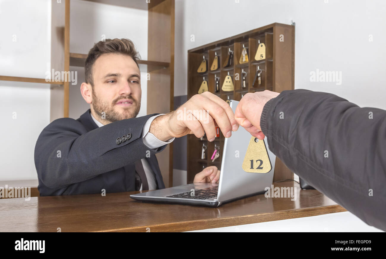 Image of a receptionist at his desk giving the key to a client ...