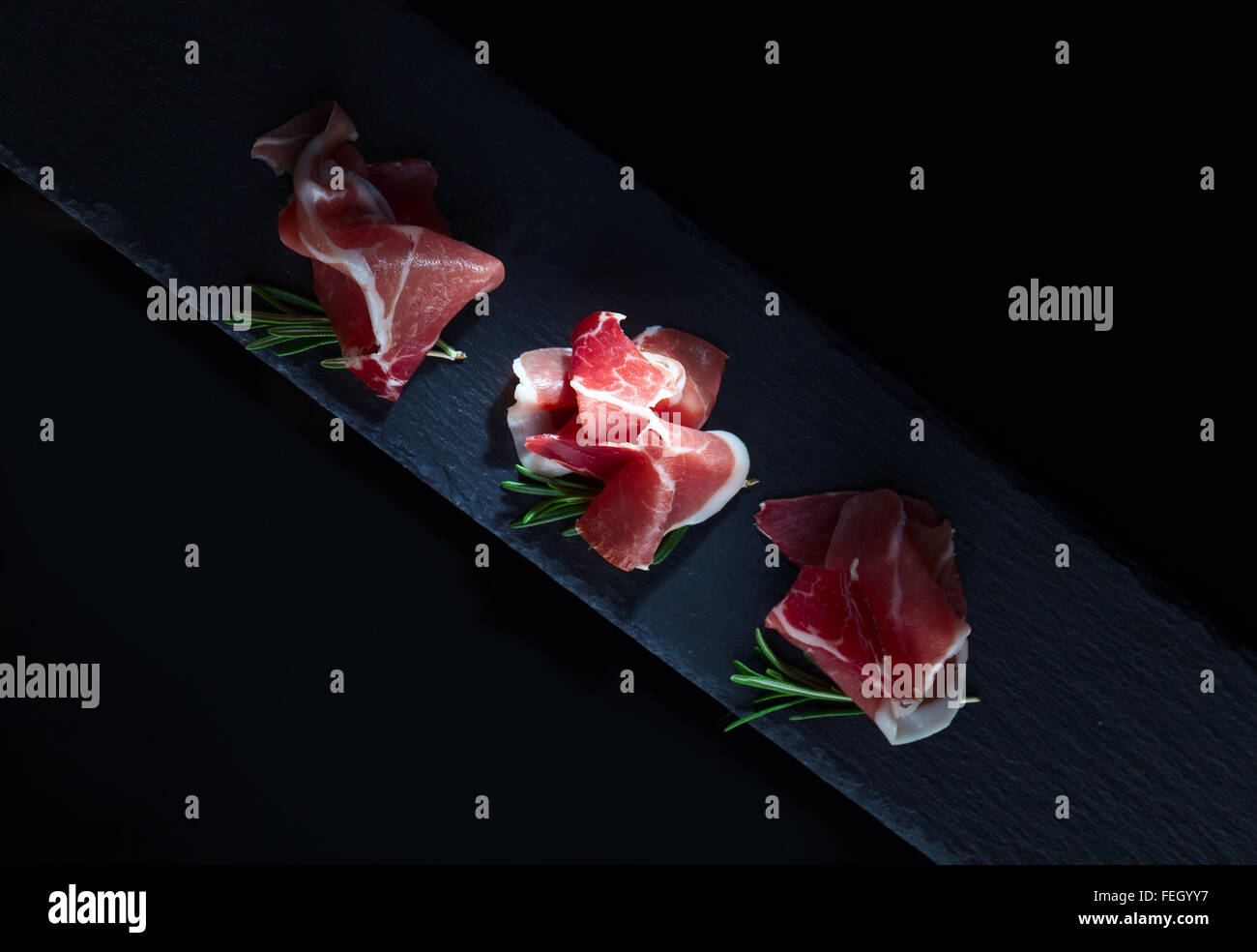 jamon with rosemary on a black background Stock Photo - Alamy