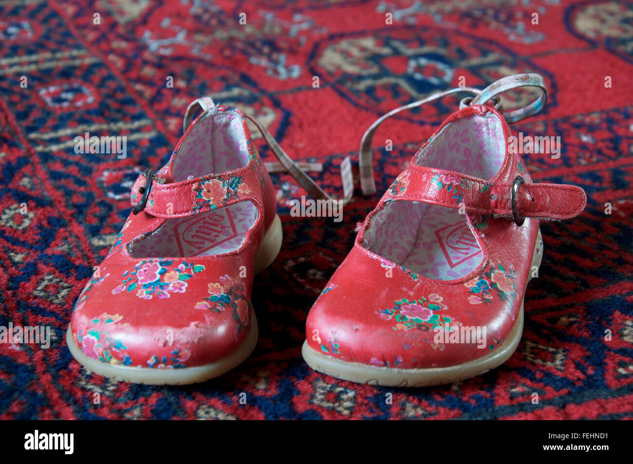 A well worn pair of little girl’s bright red shoes placed on a rug ...