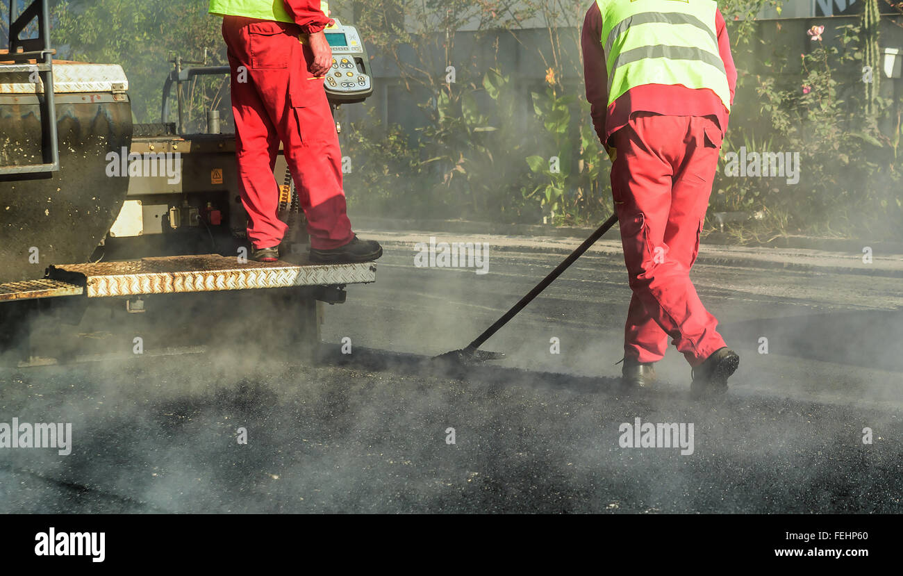 Construction worker leveling fresh asphalt pavement during road repair ...