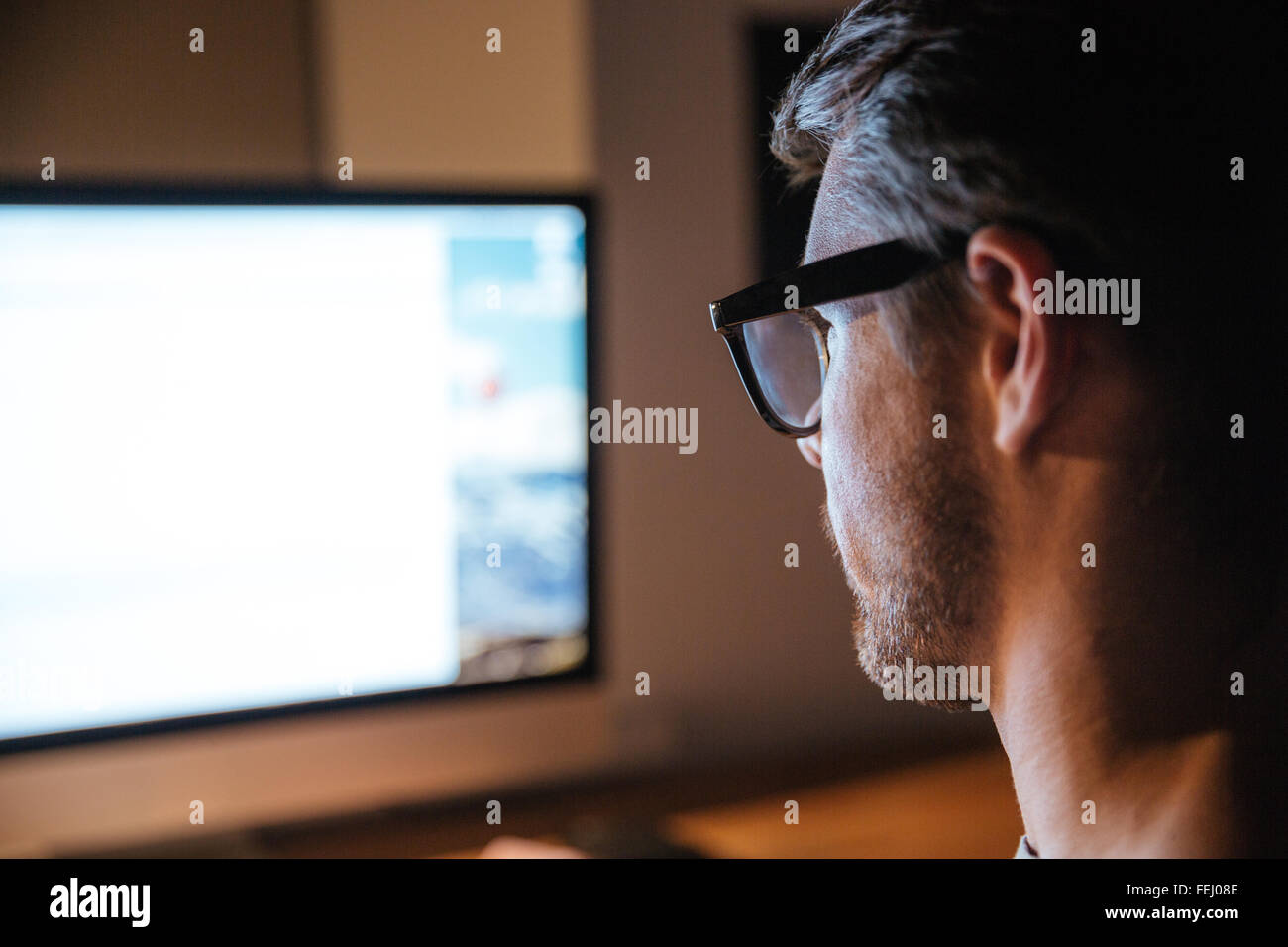 Concentrated bristled young man in glasses sitting and looking at ...