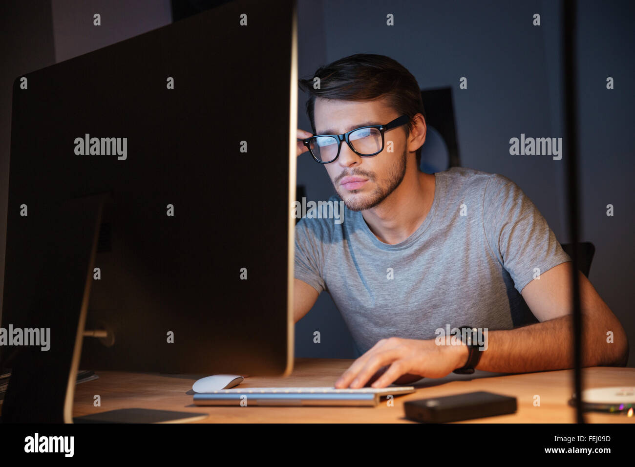 Thoughtful young man in glasses thinking and working with computer in ...