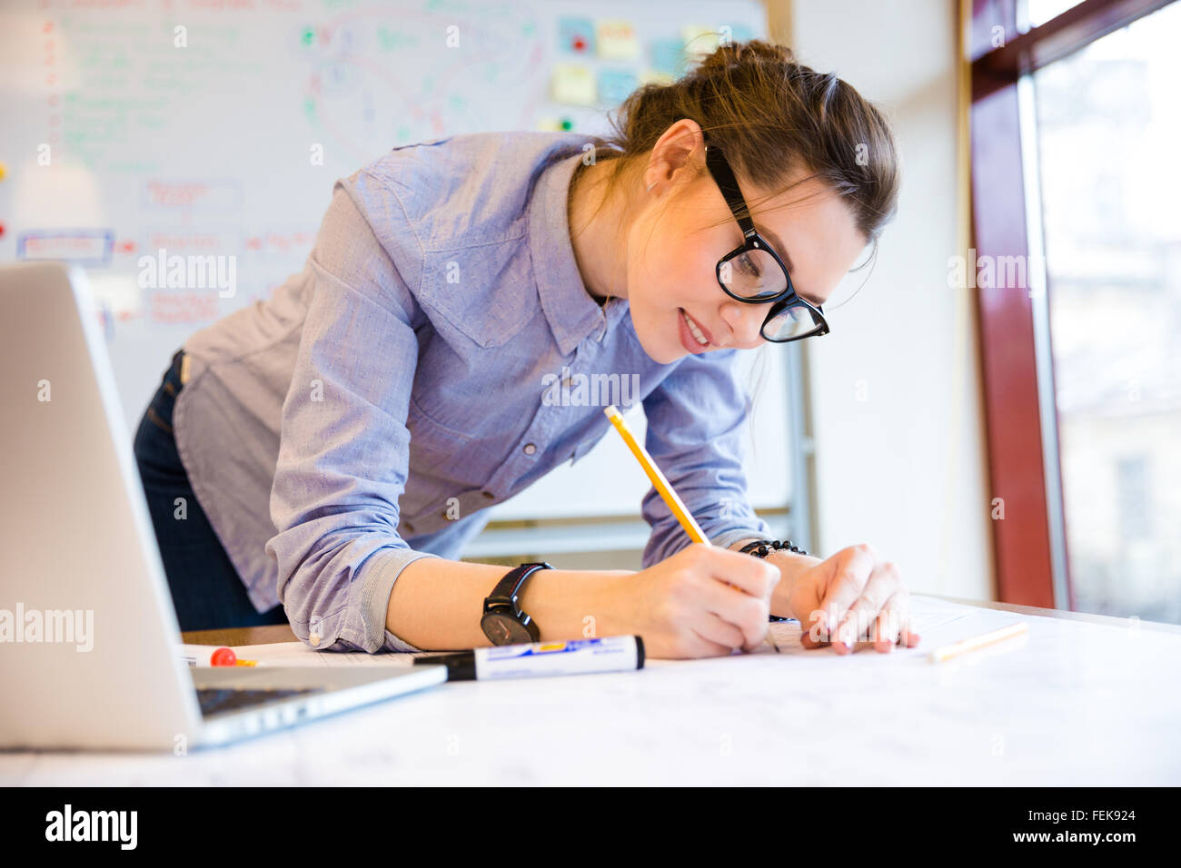 Smiling pretty young woman drawing blueprint on the table near the ...