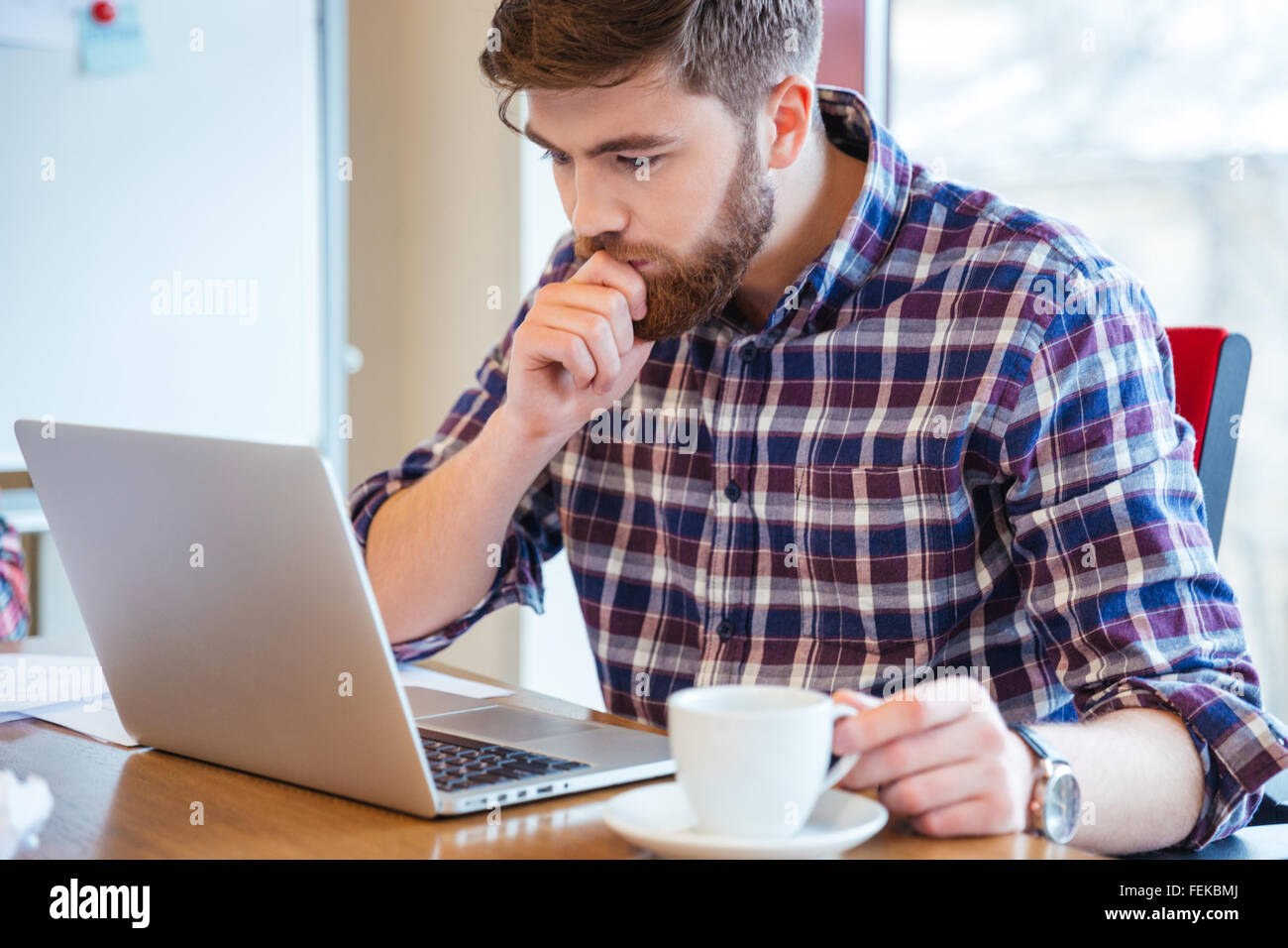 Serious Focused Bearded Young Man In Checkered Shirt Sitting At The