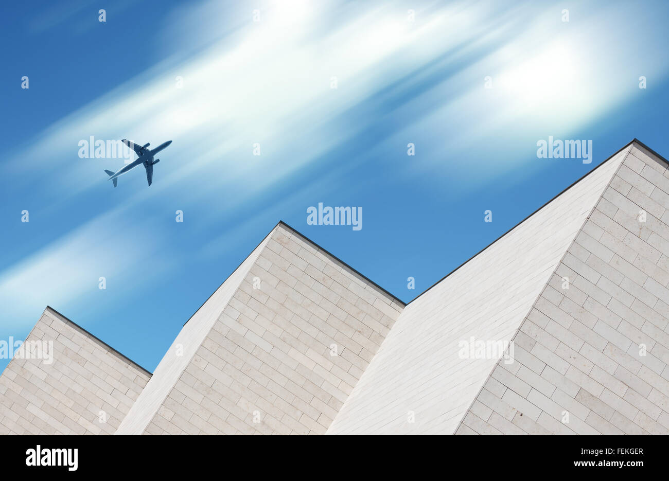 Airplane flying over modern white brick building with motion blur ...