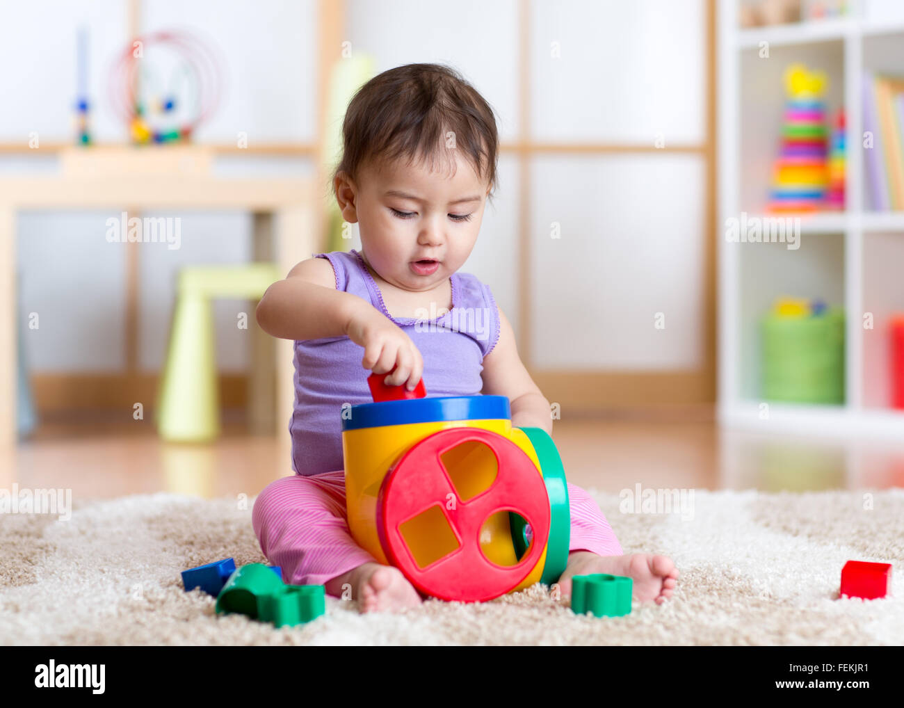 toddler girl playing indoors with sorter toy sitting on soft carpet ...