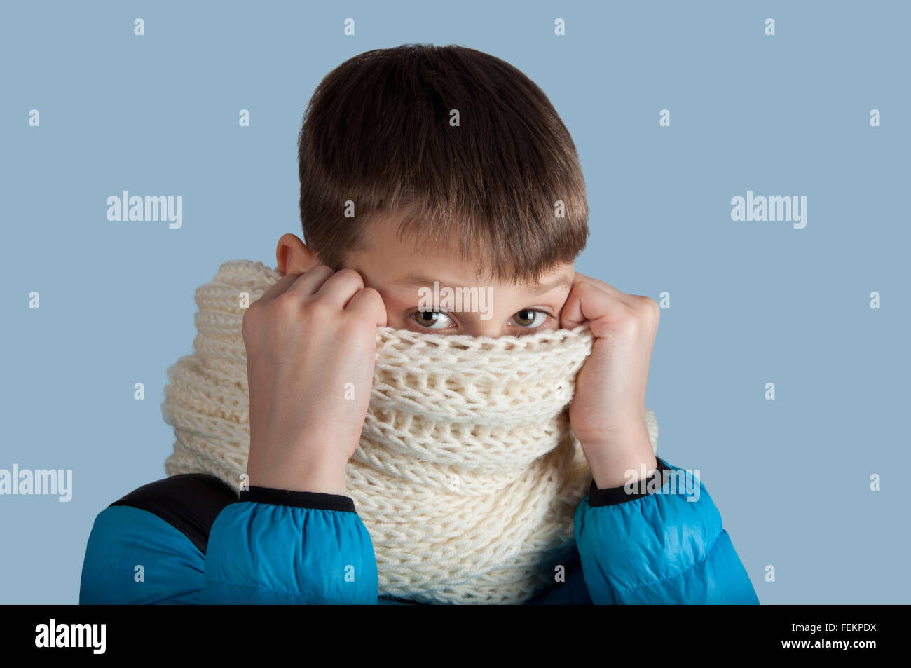 Cute boy in blue jacket and white scarf hide nose isolated on blue ...