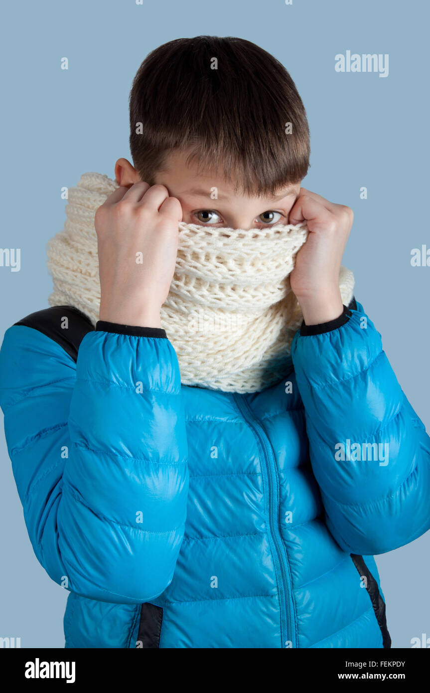 Cute boy in blue jacket and white scarf hide nose isolated on blue ...