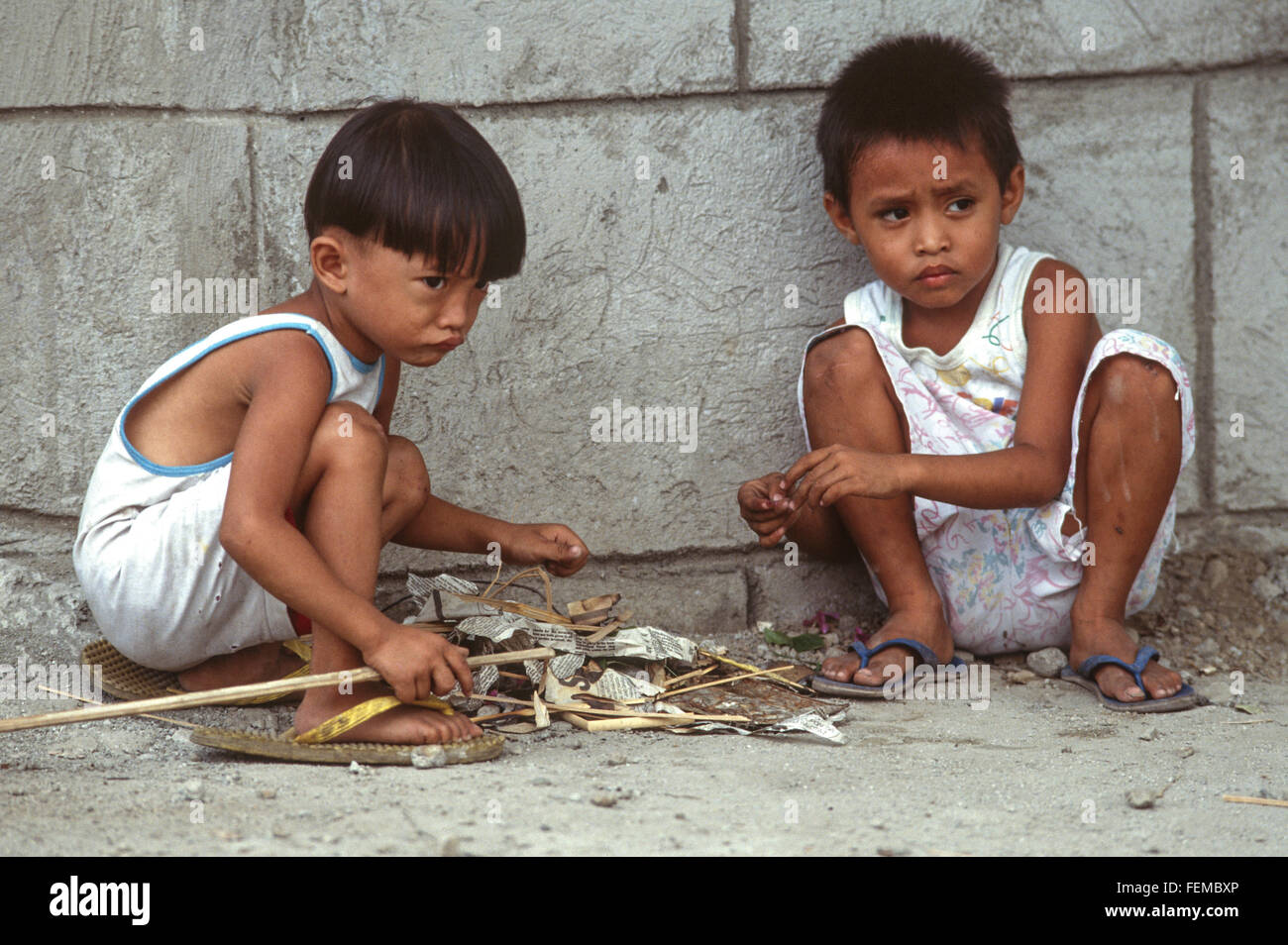 Young street children squatting by a wall collecting twigs and rubbish ...