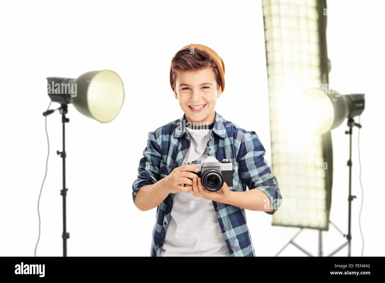 Joyful little boy holding a camera and standing in a studio with ...