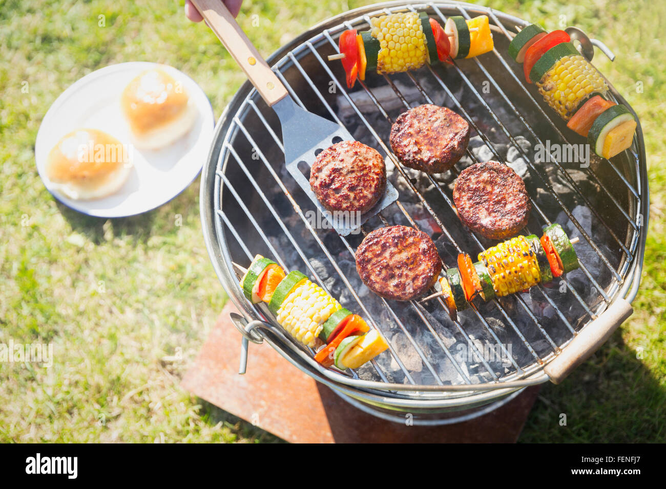 Overhead view of hamburgers and vegetable skewers on barbecue grill ...