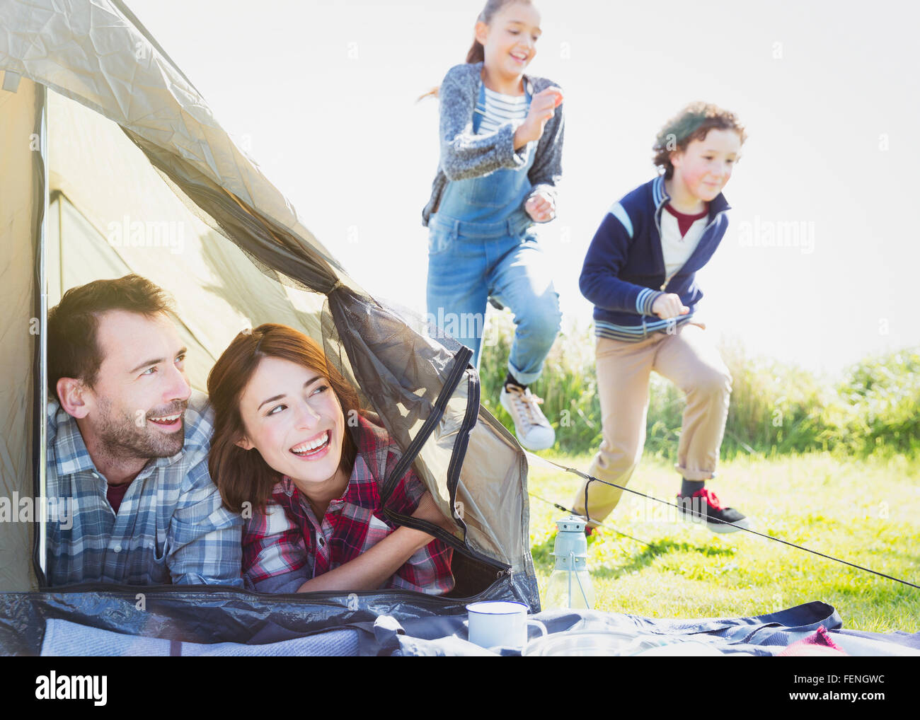 Smiling couple in tent watching kids running in grass Stock Photo - Alamy