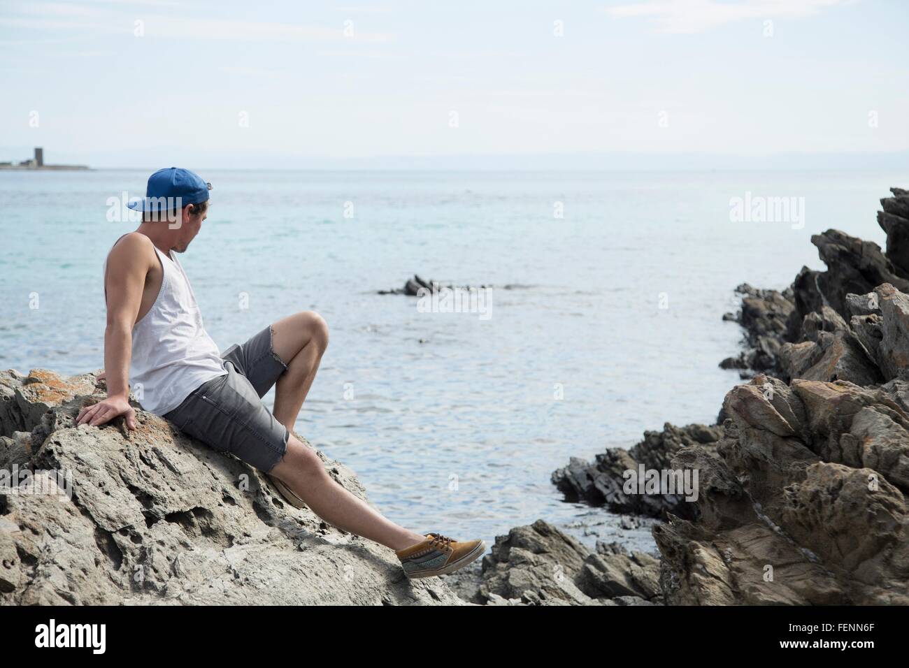 Full length side view of young man sitting on rocks looking away at ...