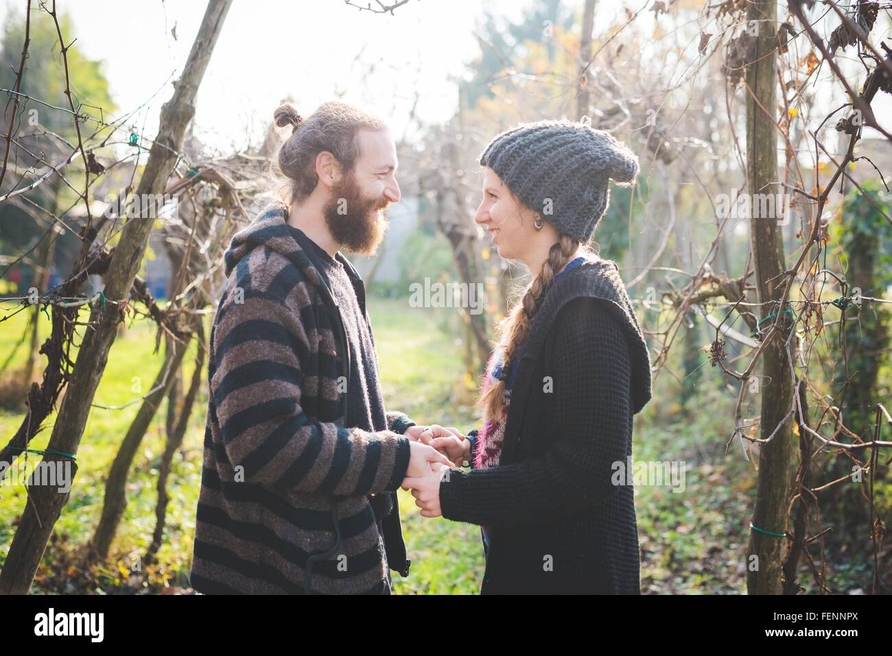 Side view of couple among trees face to face, holding hands, smiling ...