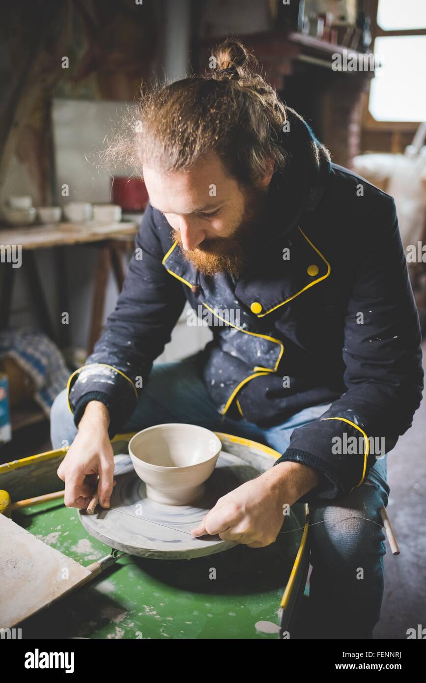 Mid adult man sitting at pottery wheel looking down at clay pot Stock ...